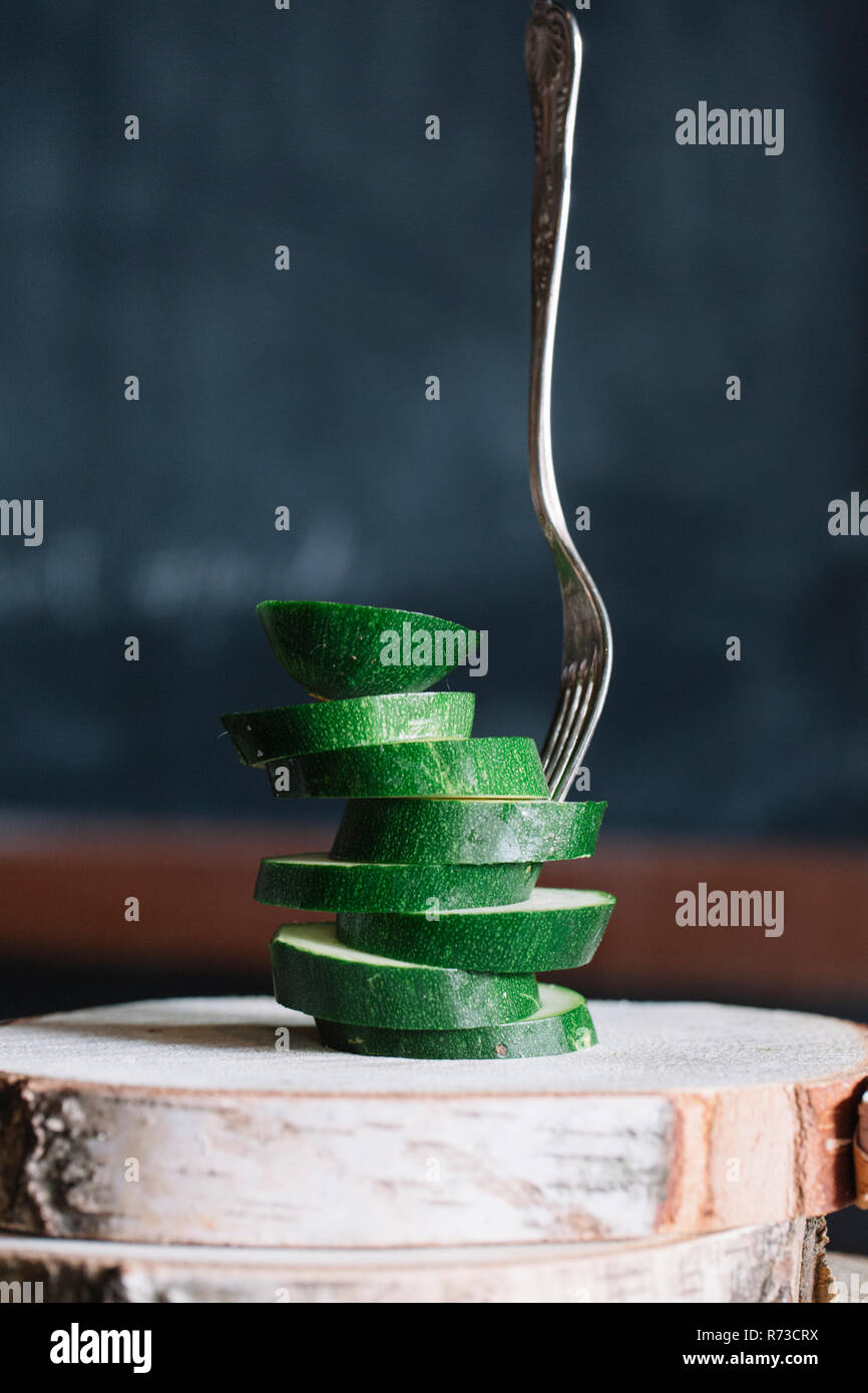 Stacked sliced courgettes and fork on rustic cutting board Stock Photo ...