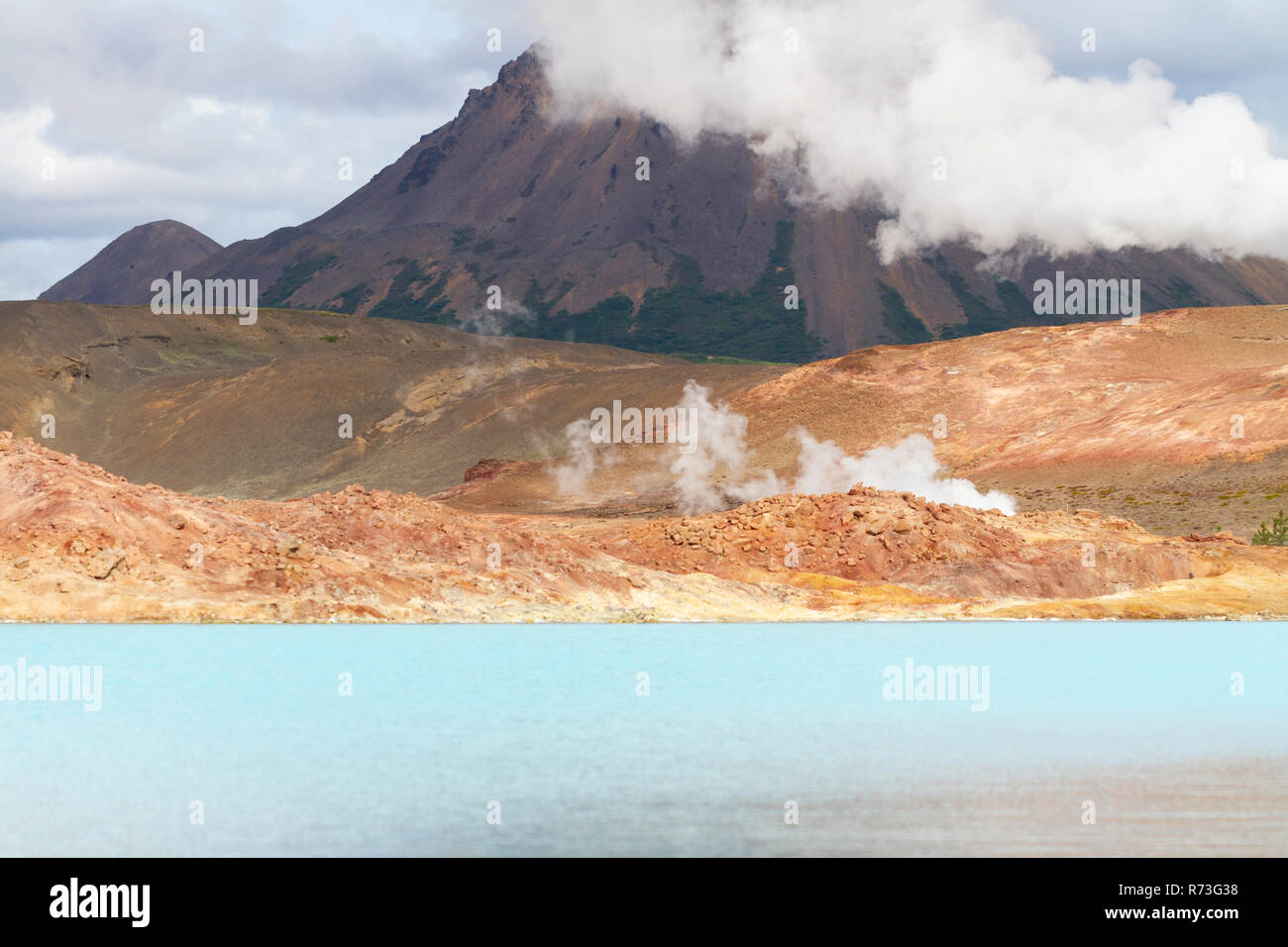 blue geothermal lake in volcanic zone with the cone of a volcano in the ...