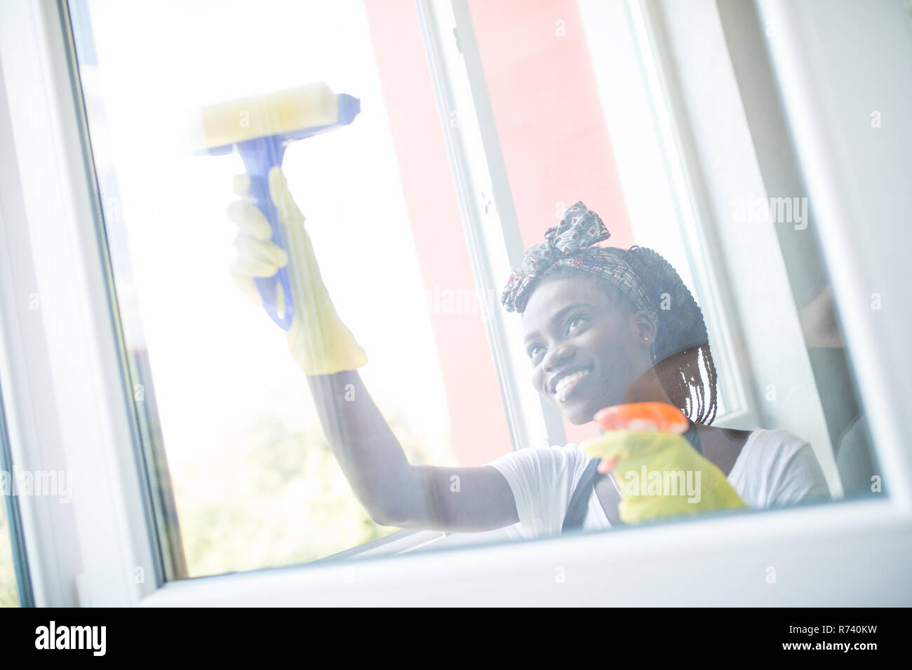Young african woman in yellow gloves cleaning window with spray ...