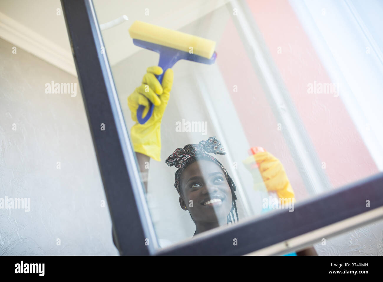 Young african woman in yellow gloves cleaning window with spray ...