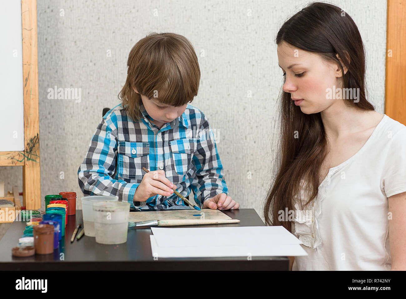 Young beautiful mother with boys son paint colors at home. Mom teaches ...