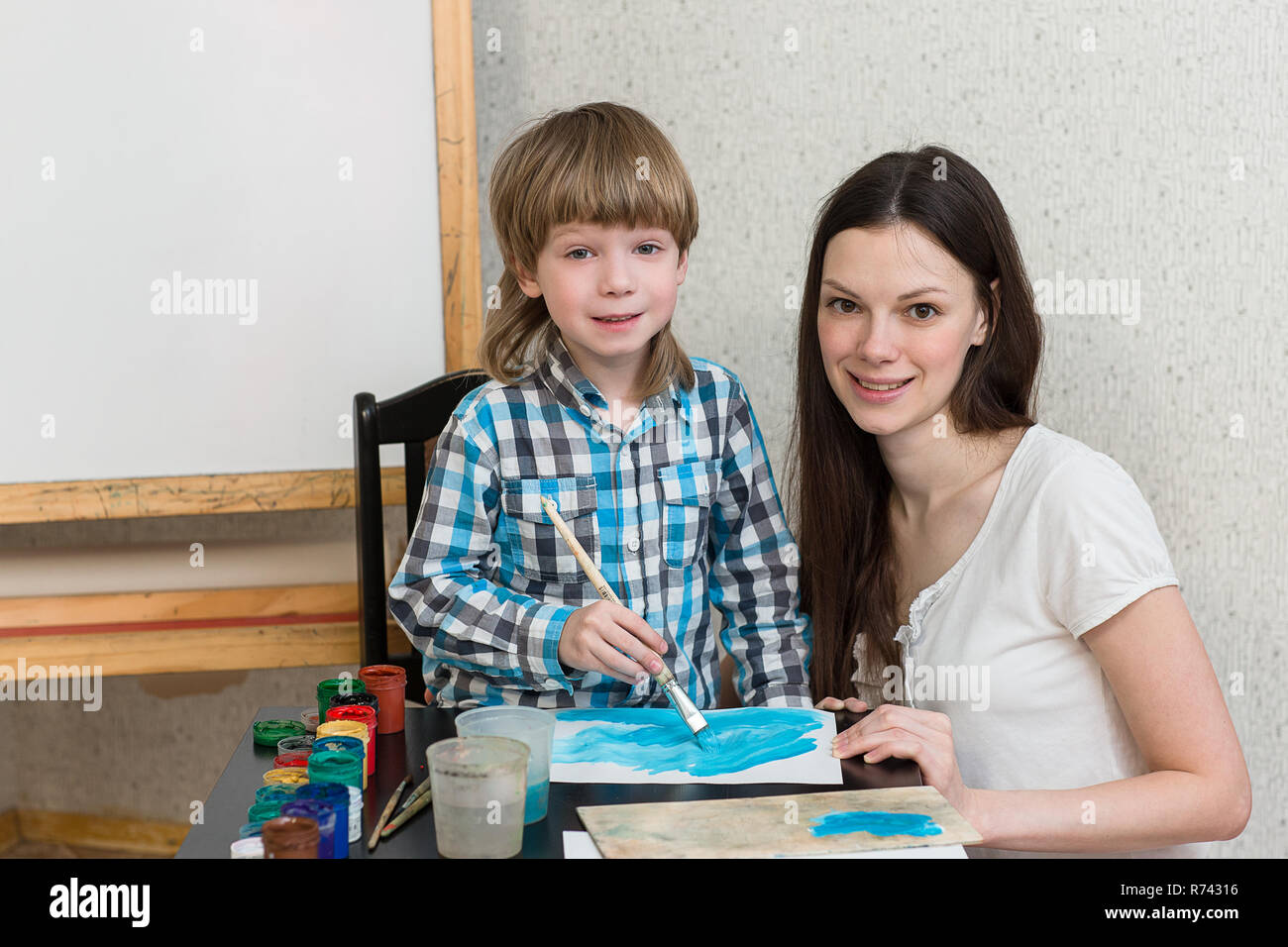 Young beautiful mother with boys son paint colors at home. Mom teaches ...
