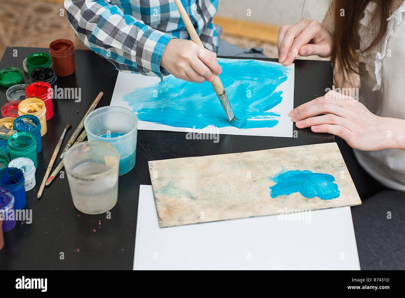 Young beautiful mother with boys son paint colors at home. Mom teaches ...