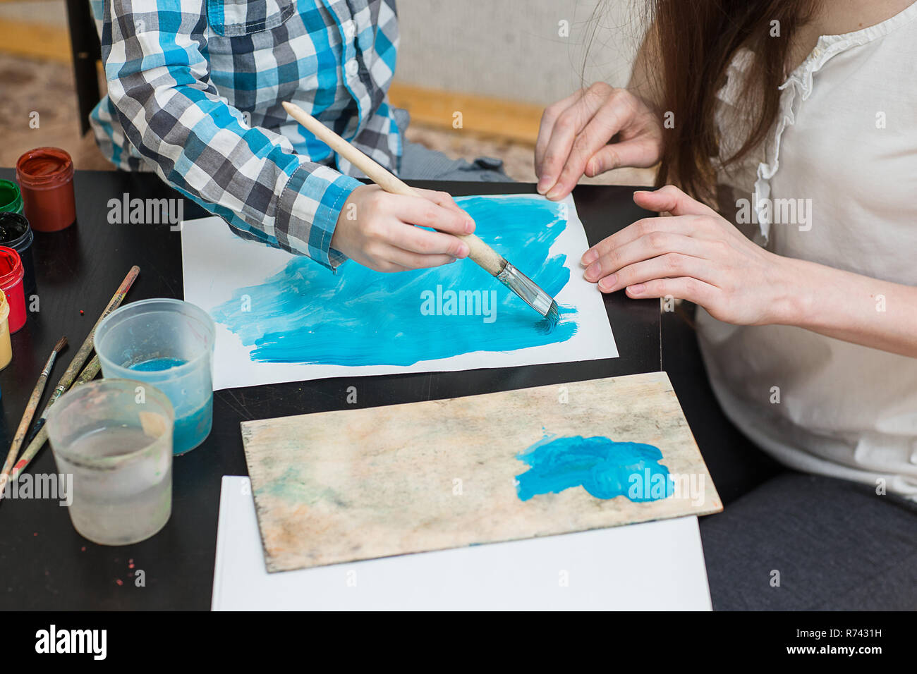 Young beautiful mother with boys son paint colors at home. Mom teaches ...