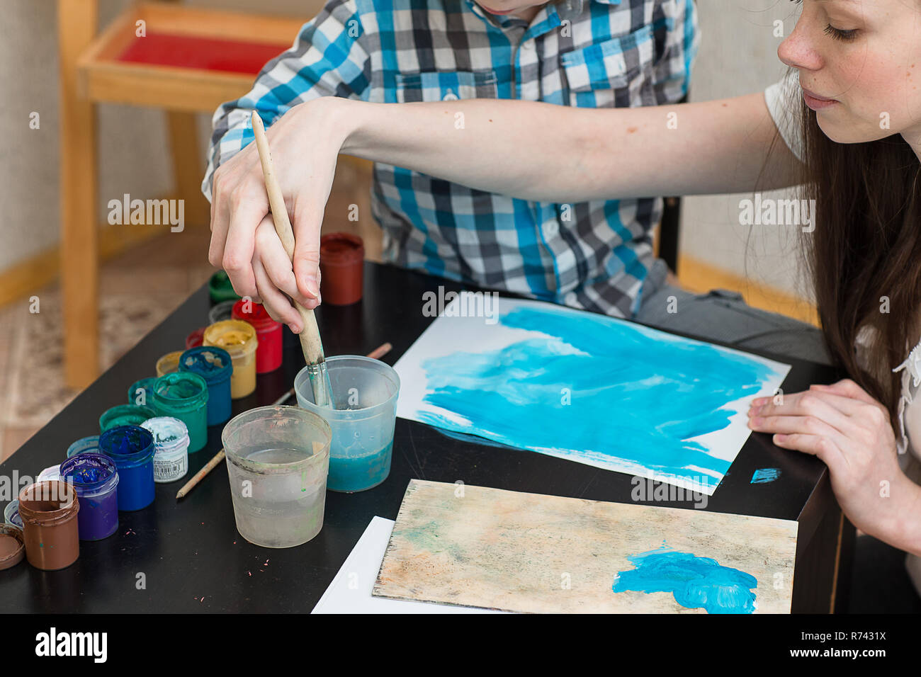 Young beautiful mother with boys son paint colors at home. Mom teaches ...