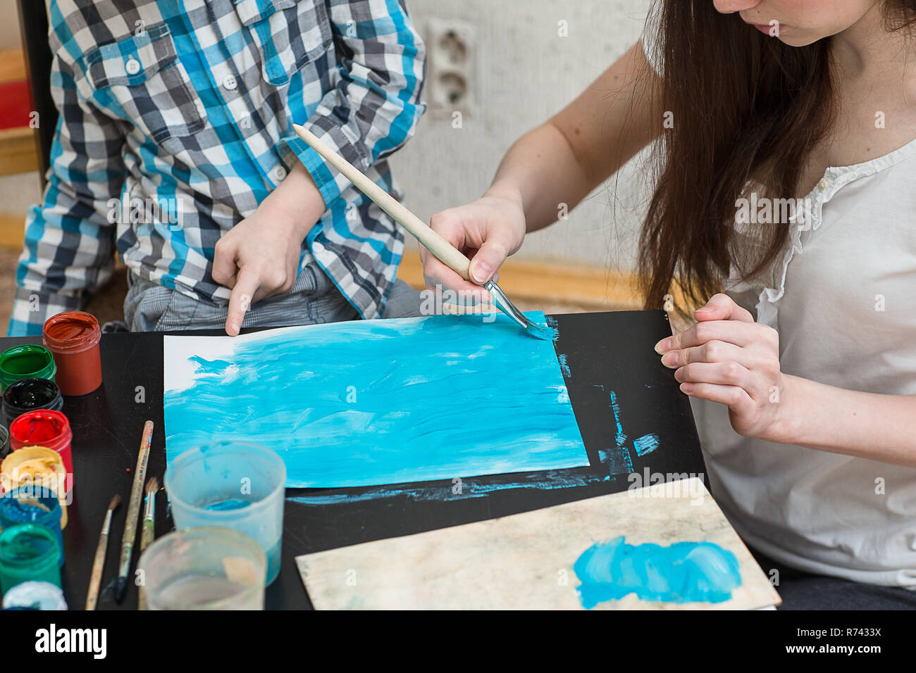 Young beautiful mother with boys son paint colors at home. Mom teaches ...