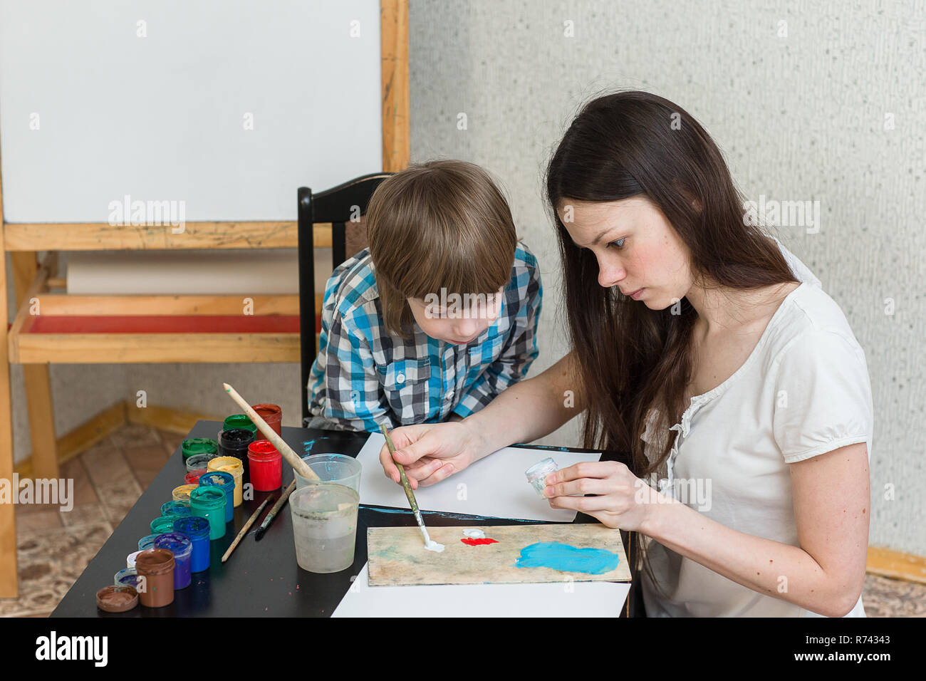 Young beautiful mother with boys son paint colors at home. Mom teaches ...