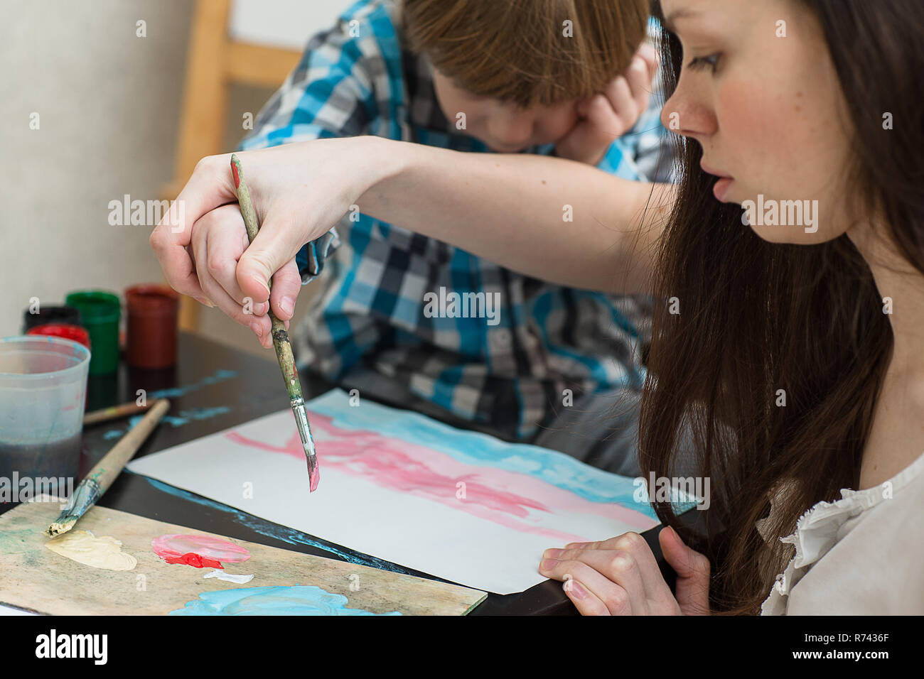 Young beautiful mother with boys son paint colors at home. Mom teaches ...