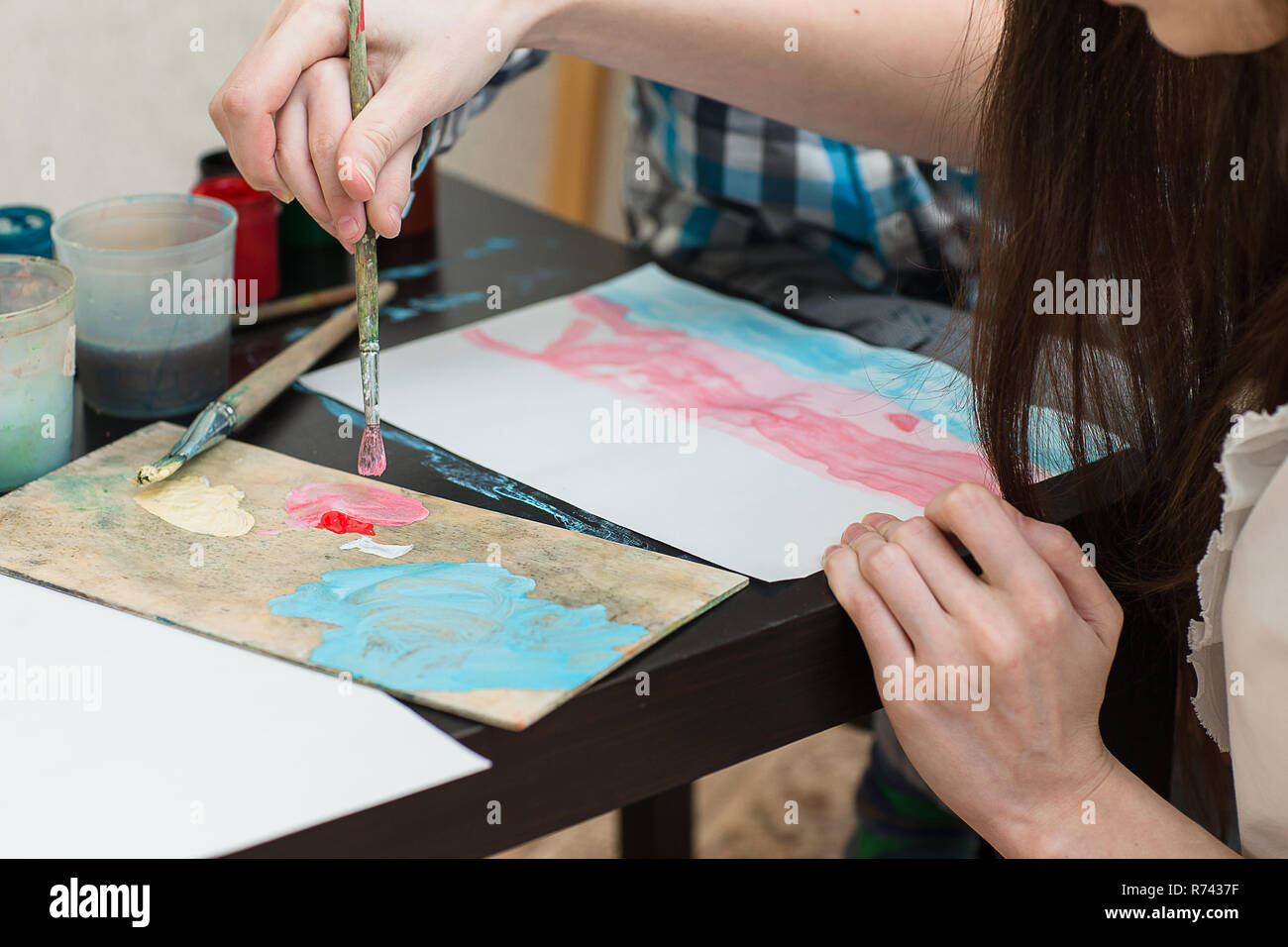 Young beautiful mother with boys son paint colors at home. Mom teaches ...