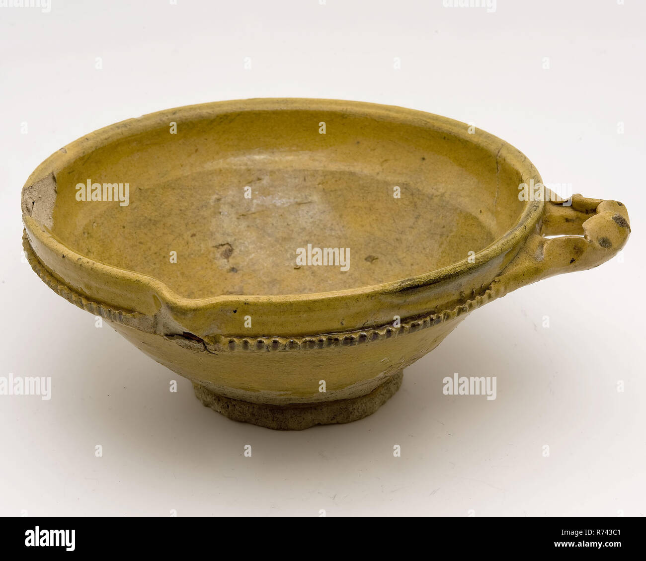 Yellow earthenware bowl with pinched lying ear, pouring lip, ribbed ...