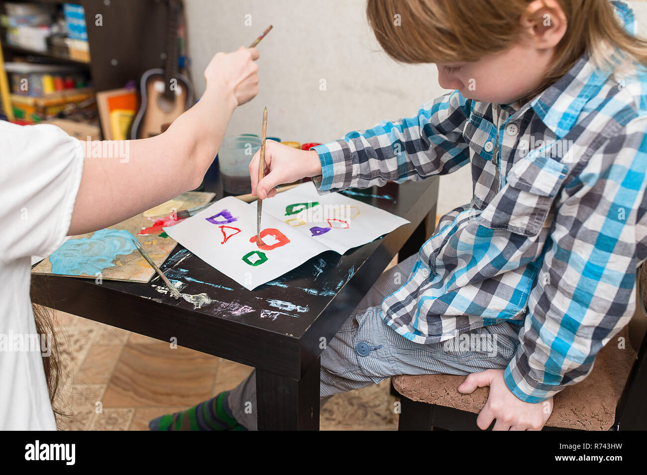 Young beautiful mother with boys son paint colors at home. Mom teaches ...