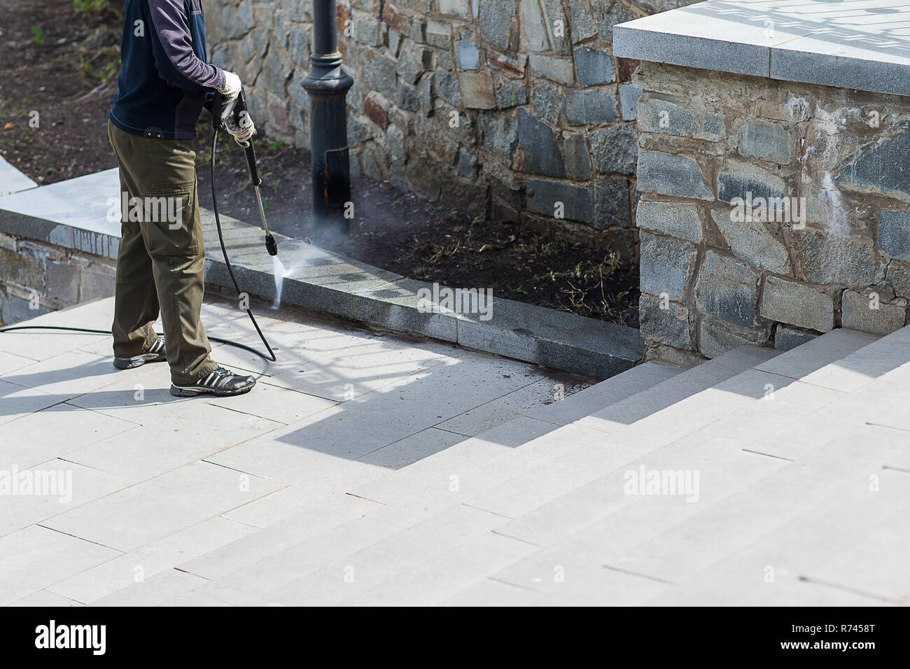 Construction worker cleaning street with water hose Stock Photo - Alamy