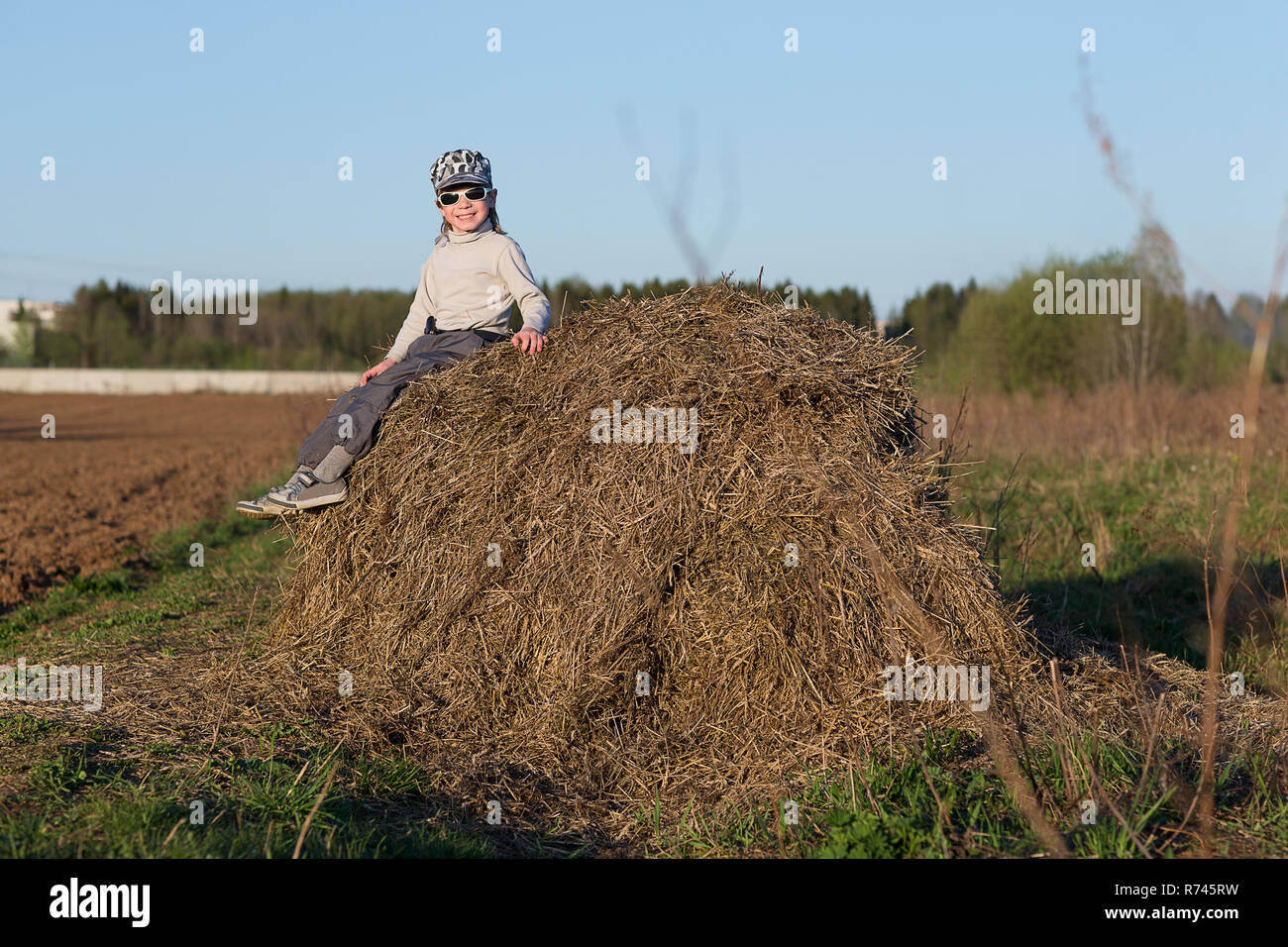 Cheerful smiling child sitting on a haystack at sunset Stock Photo - Alamy