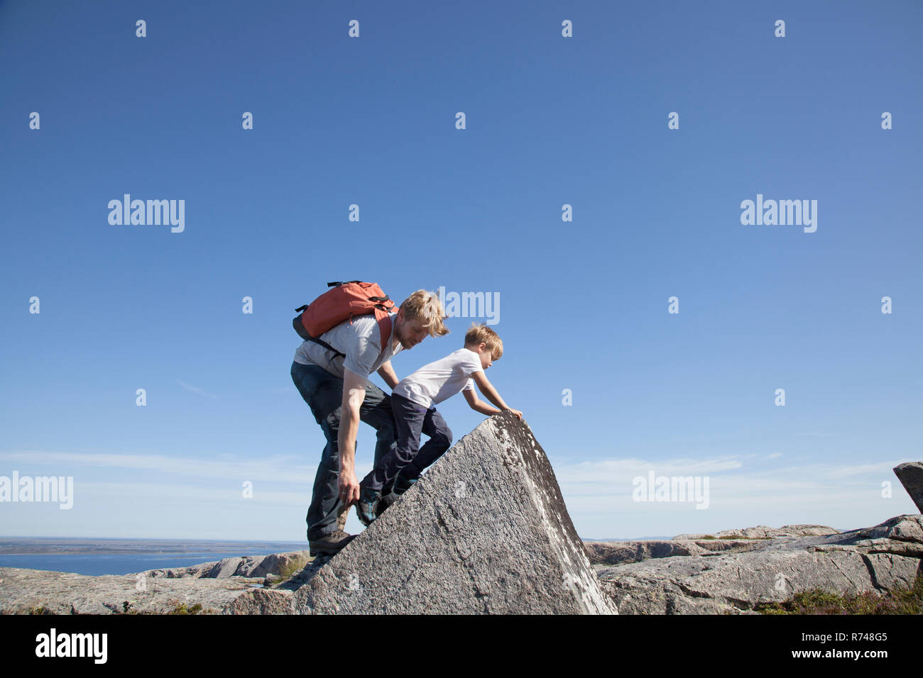 Boy and father climbing rock formation over inlet, Aure, More og ...