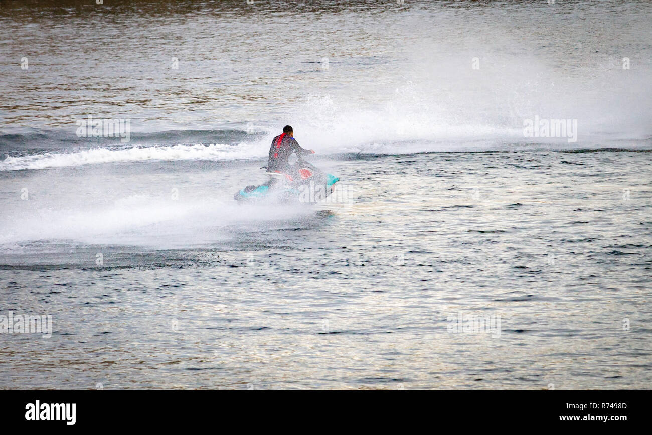A light blue speedboat with one male rider, speeds along the river ...