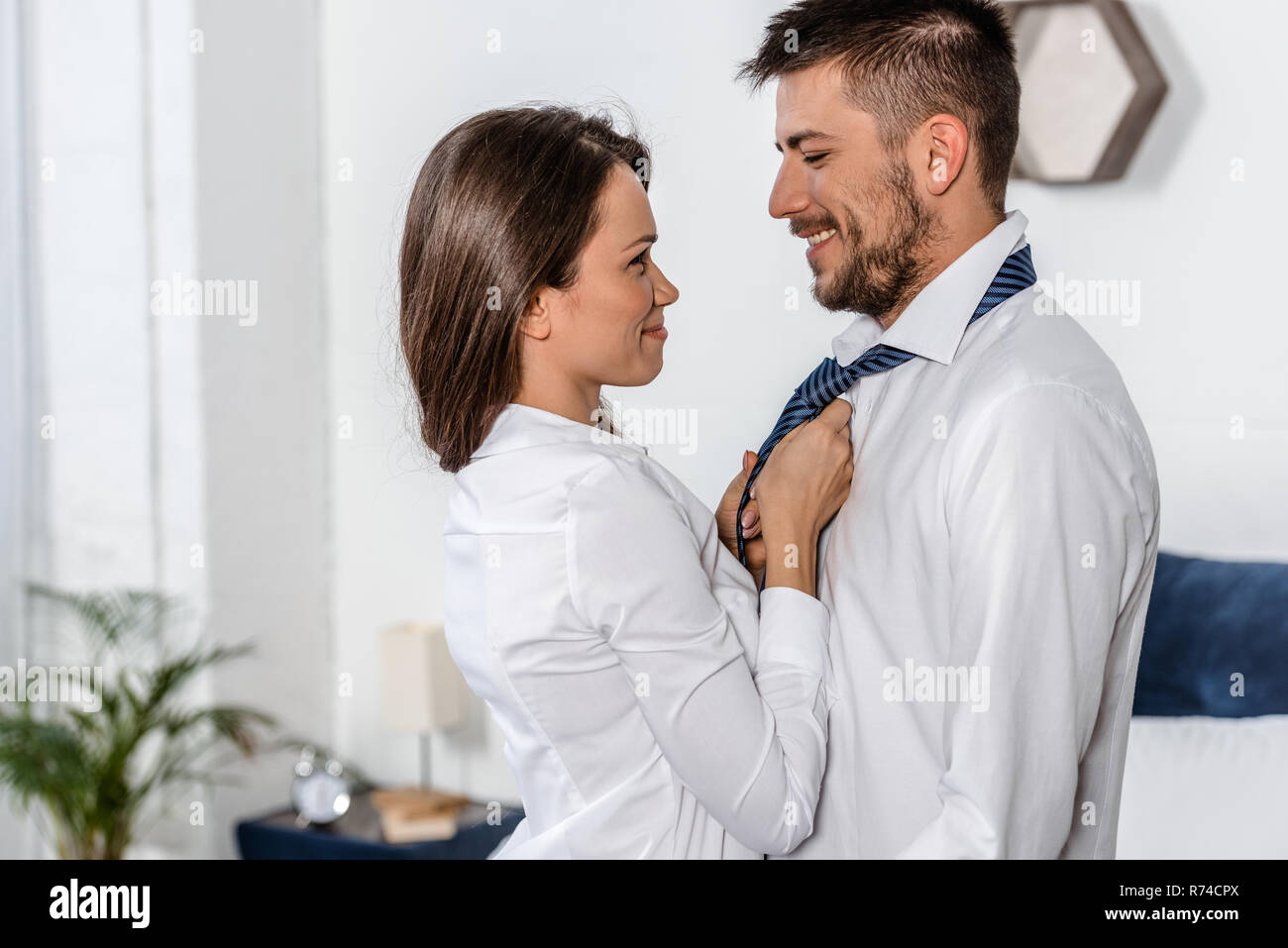 side view of cheerful girlfriend tying boyfriend tie in morning on ...