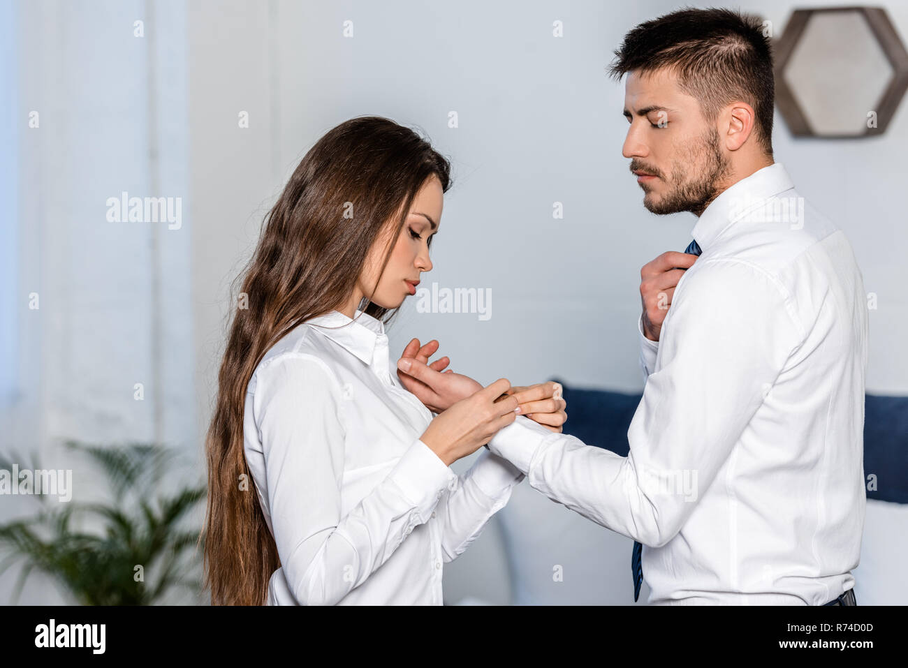 Side view of girlfriend buttoning boyfriend cuff in morning at home ...