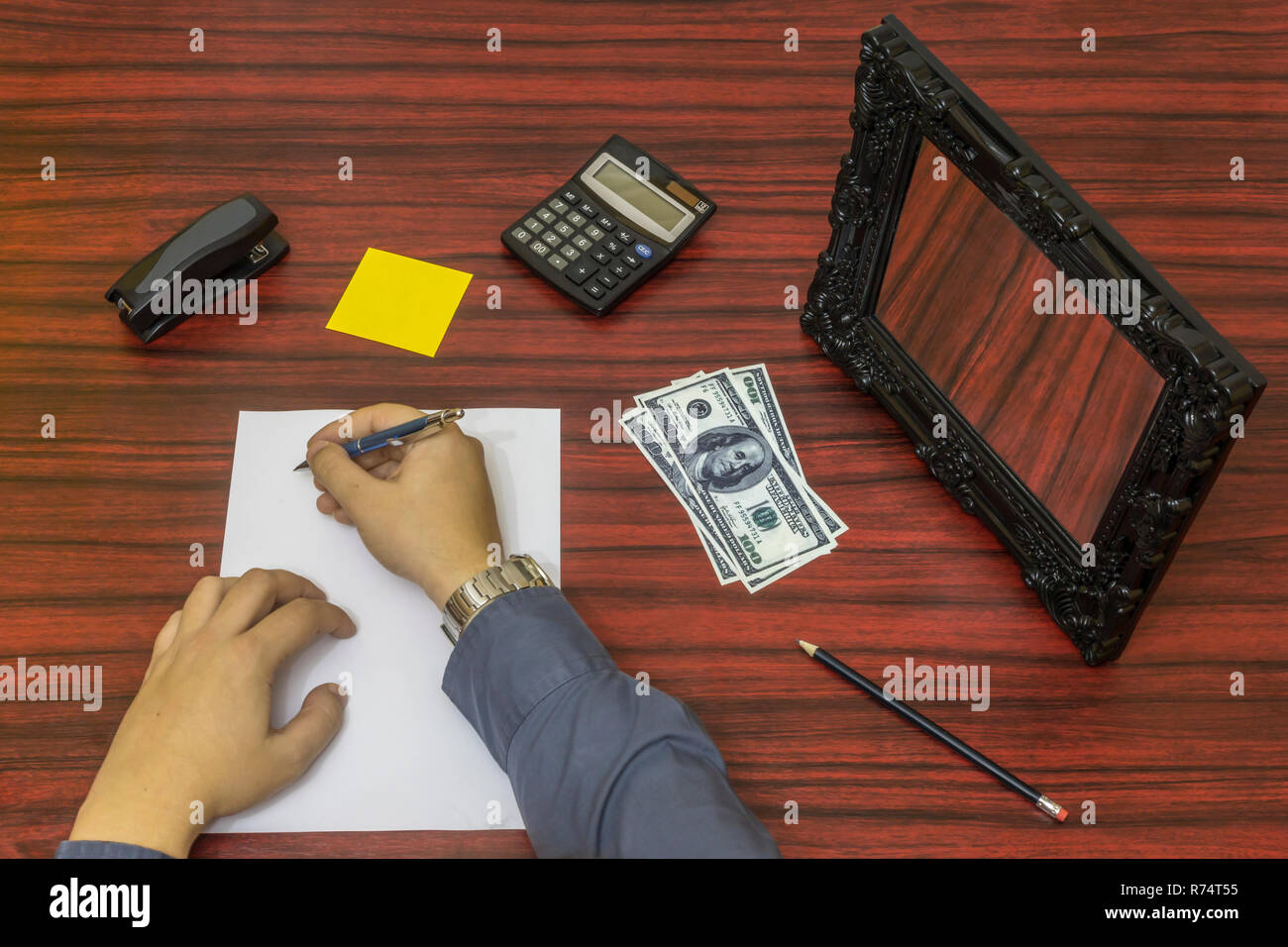 Person writing on paper. There are money lying on the desk withour ...