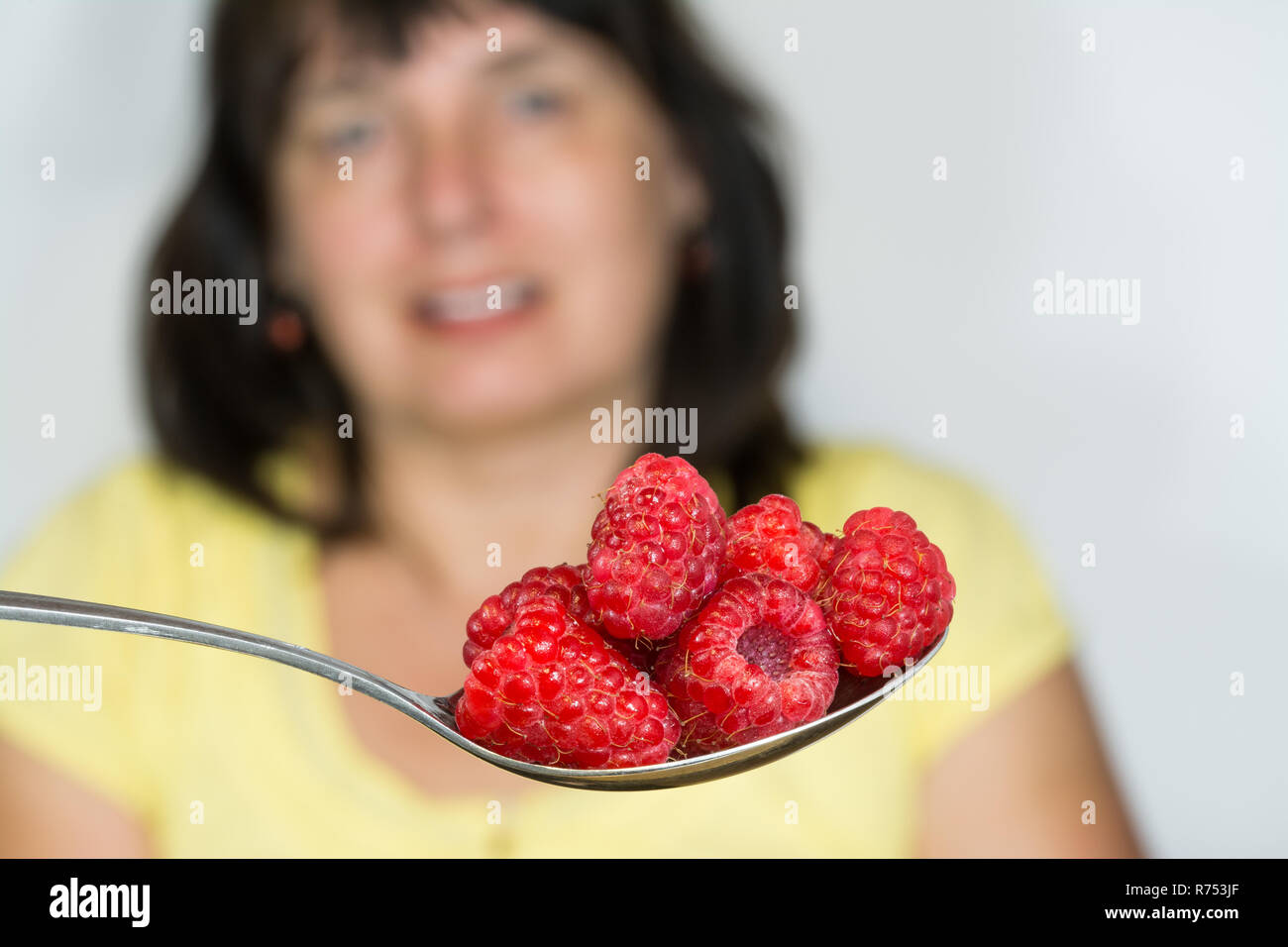 Red juicy raspberries on spoon. Blurred woman in background. Detail of ...