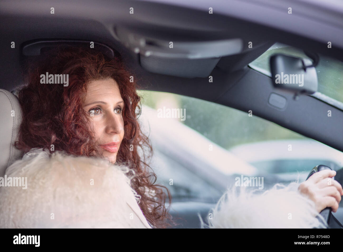 mature woman in white fur driving car and looking to passenger Stock ...