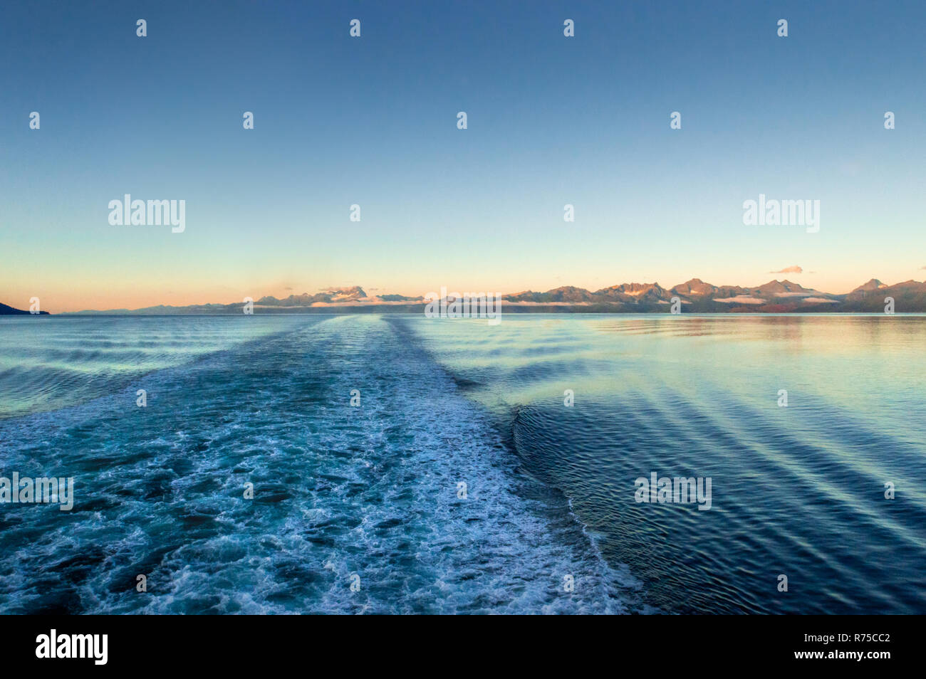Ship's ocean wake at dawn with sunrise light upon rugged mountains ...