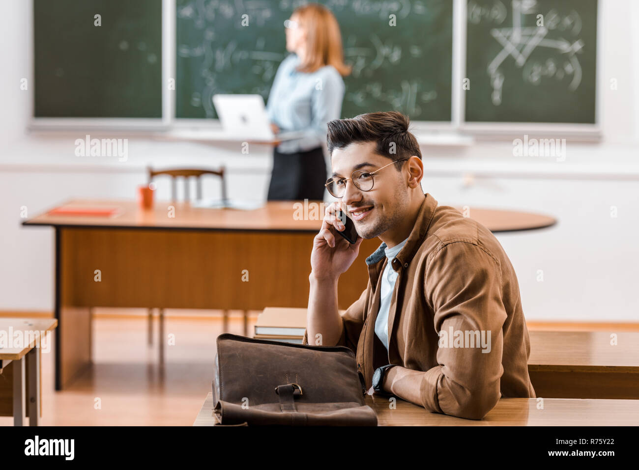 Student talking on smartphone in classroom with lecturer on background ...
