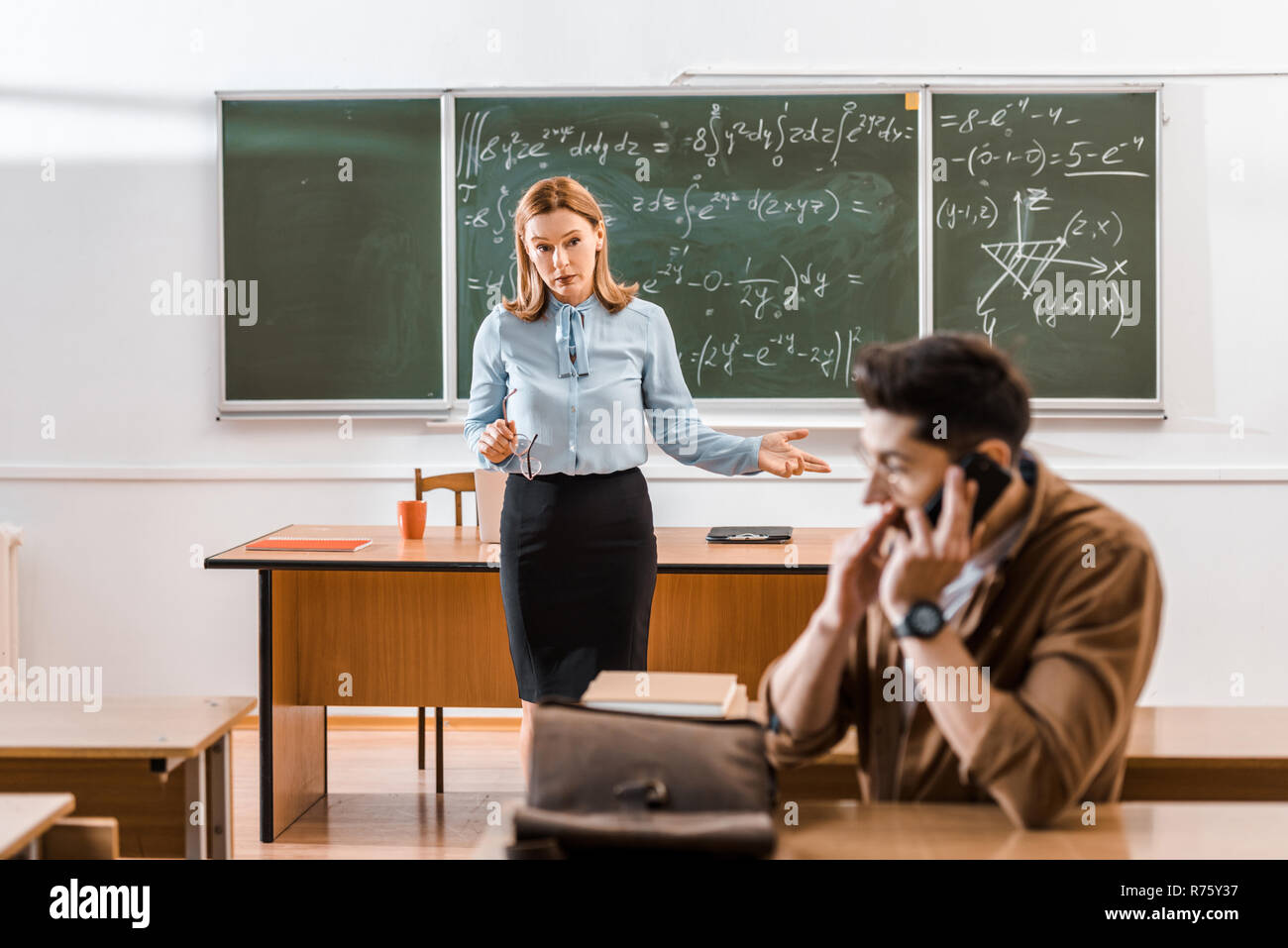 dissatisfied teacher looking at student who talking on smartphone in ...