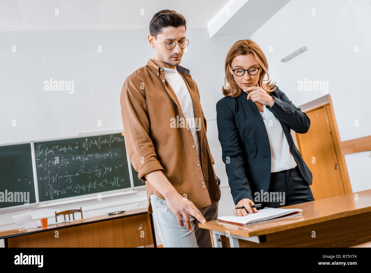 focused female teacher helping male student with assignment during ...