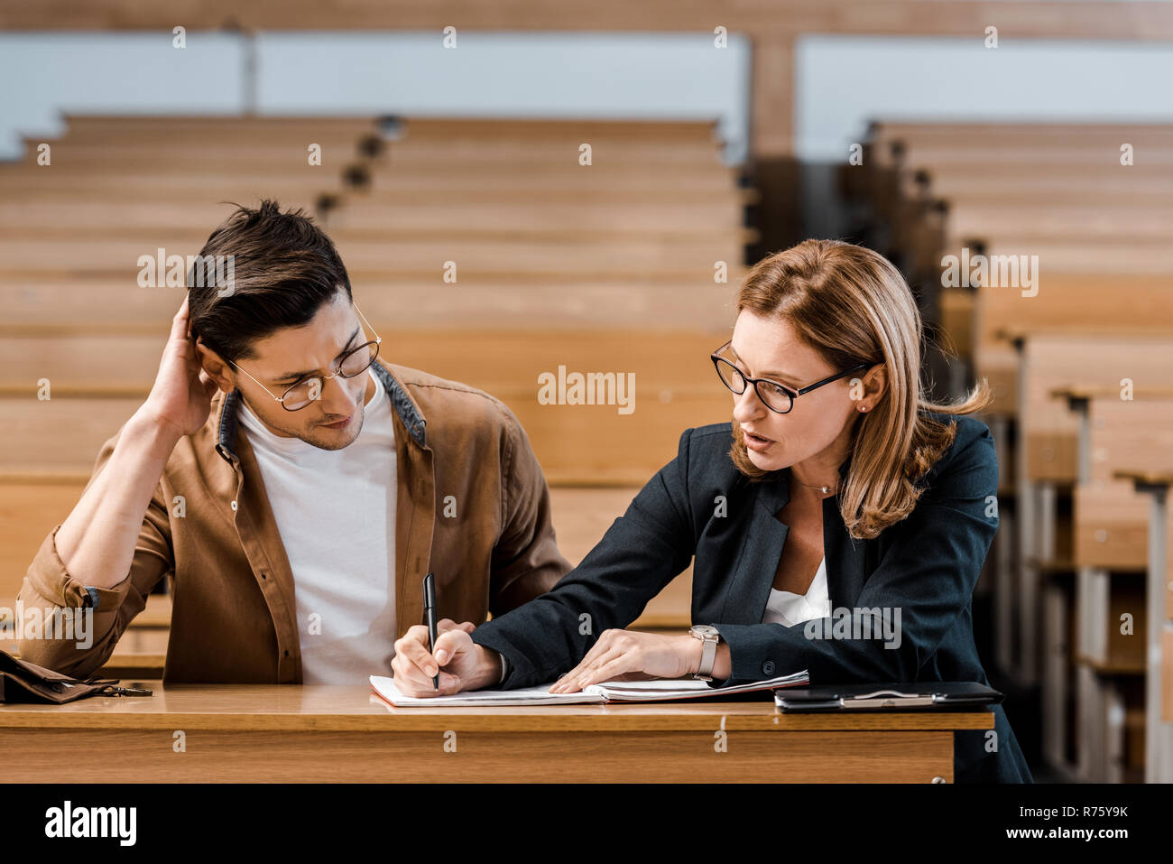 female teacher checking exam results of male student in classroom Stock ...