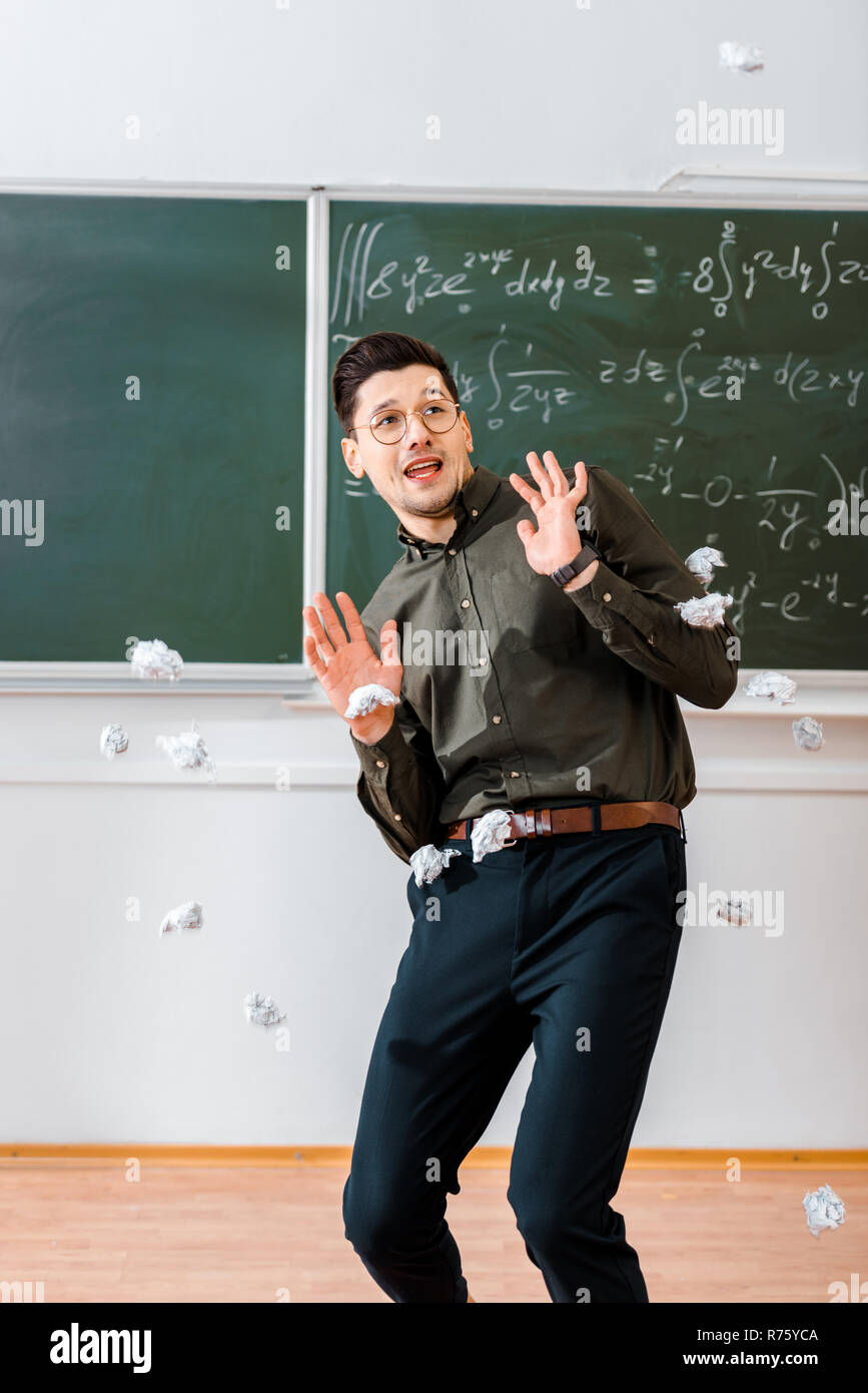 crumpled paper balls flying at frightened male teacher in classroom ...