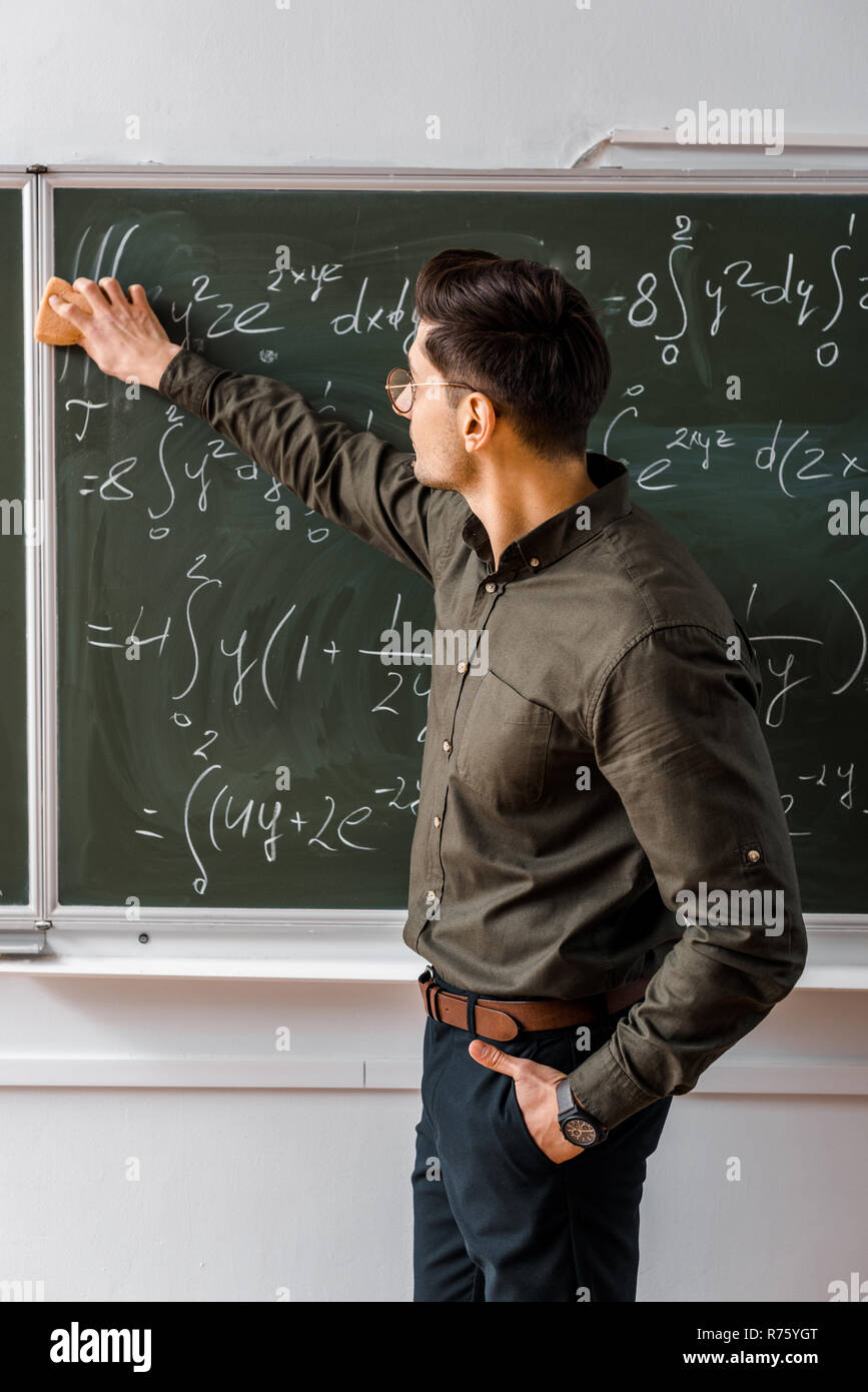 male teacher wiping mathematical equations with sponge from chalkboard ...