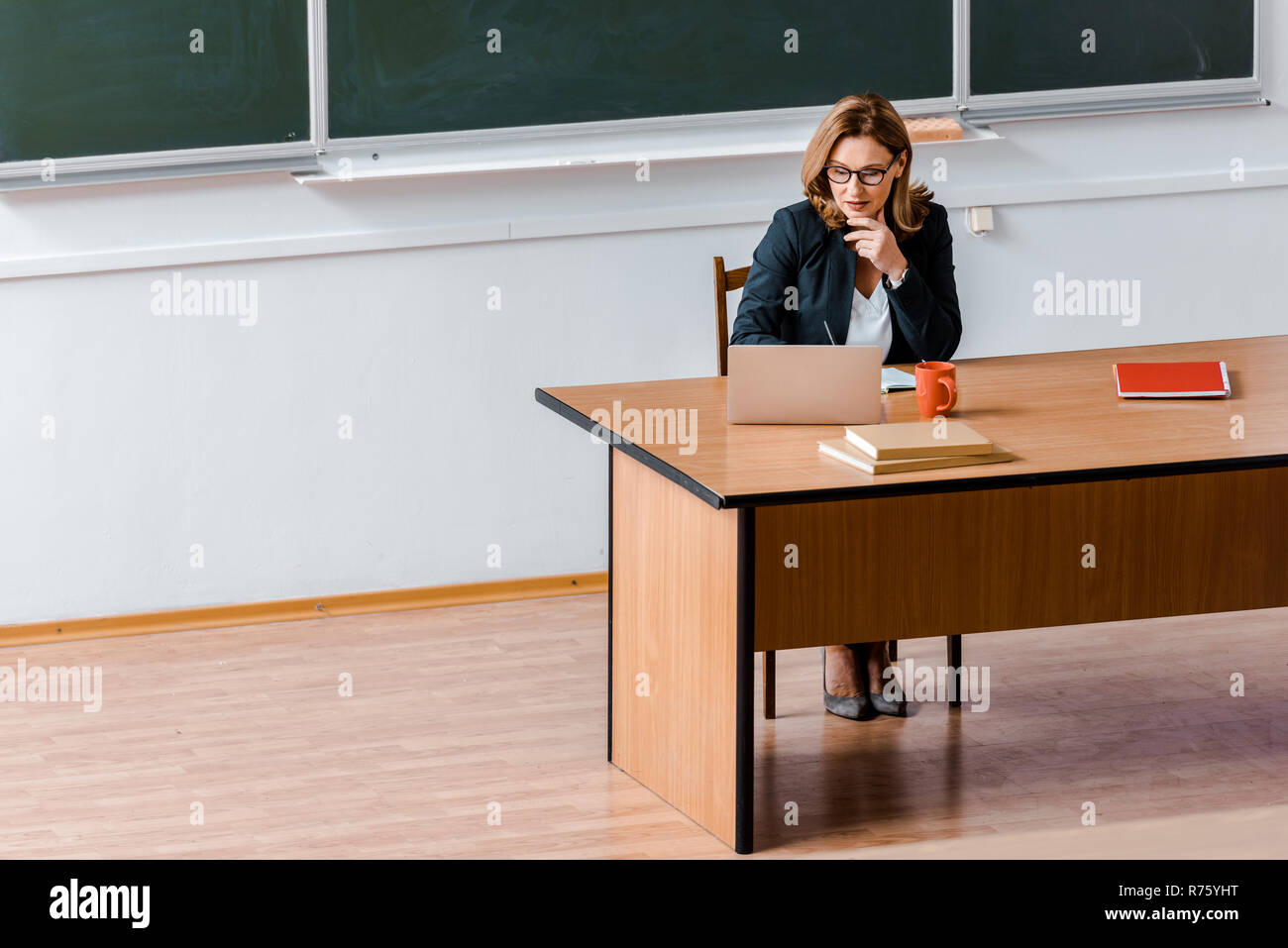 female university professor in glasses sitting at desk and using laptop ...