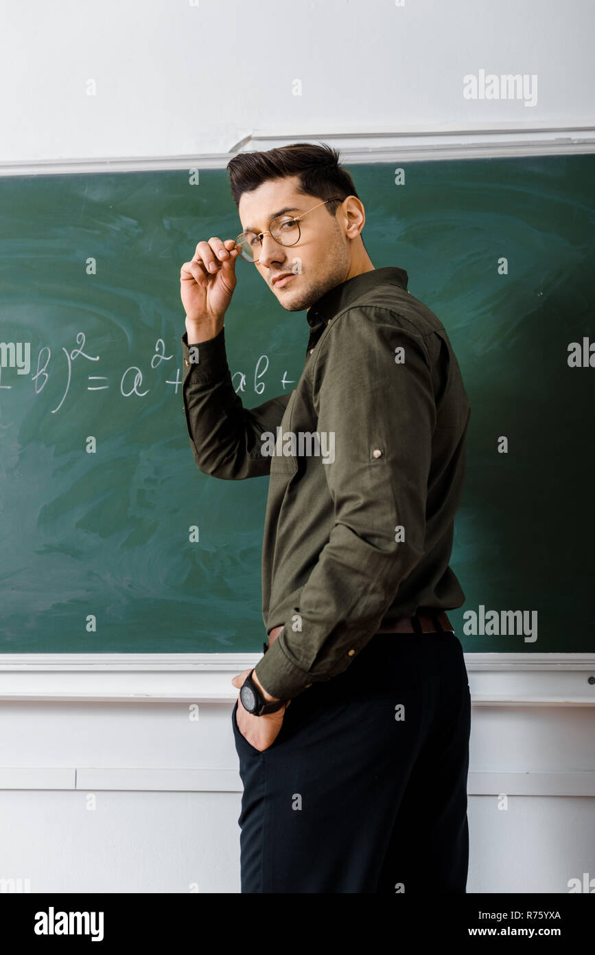 handsome male teacher holding glasses and looking at camera in maths ...