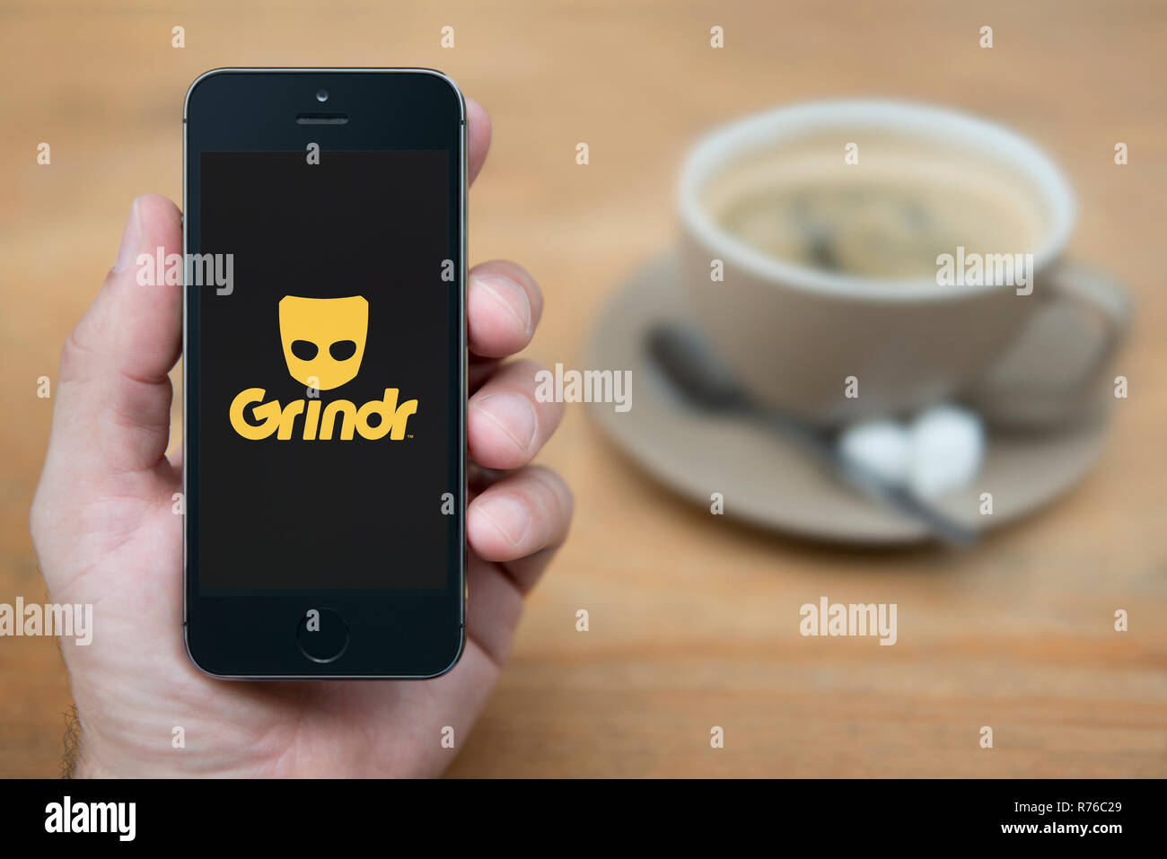A man looks at his iPhone which displays the Grindr logo (Editorial use ...