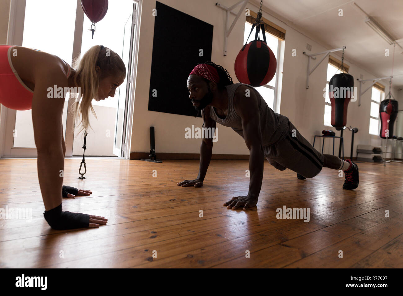 Trainer assisting female boxer in doing push ups in fitness studio ...
