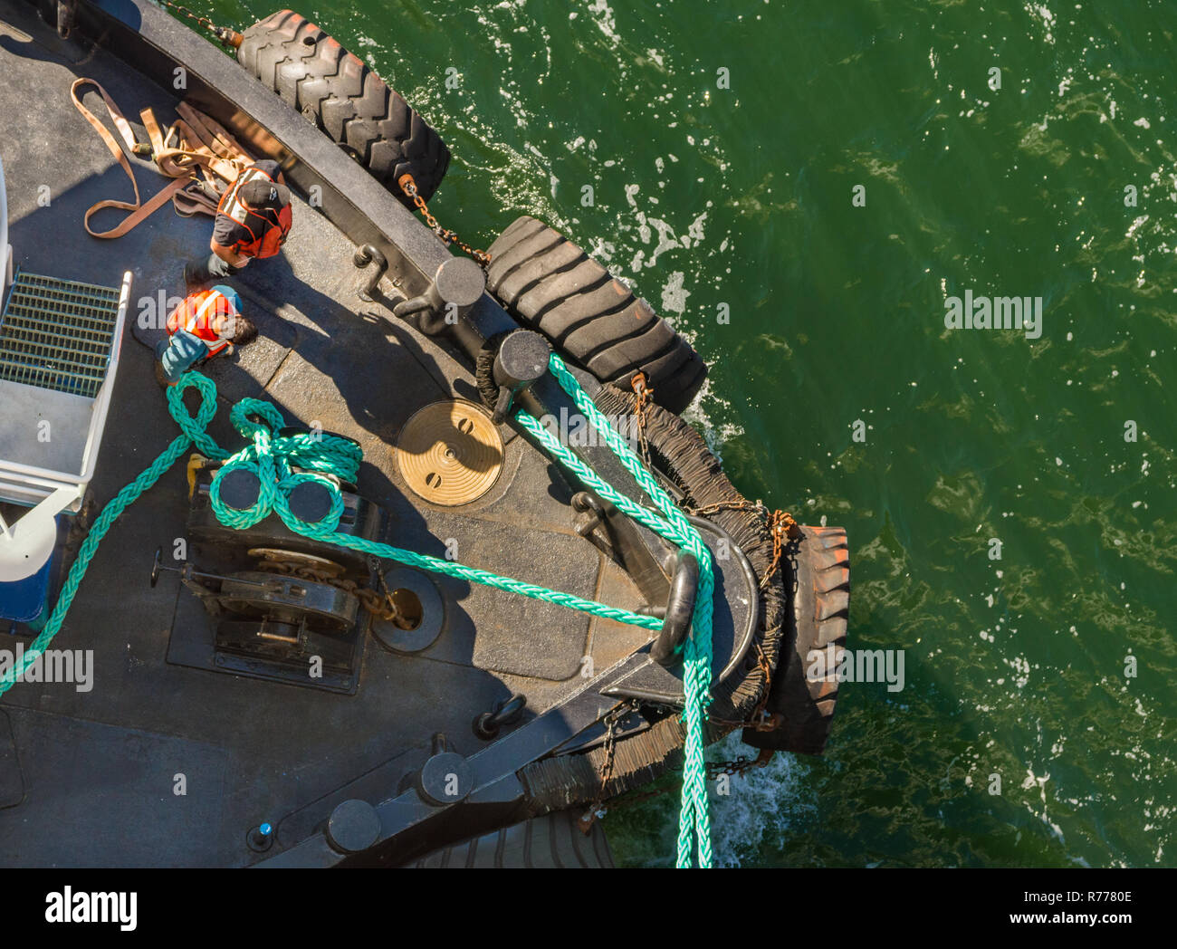 Overhead POV view of tugboat, ropes and workers assisting large ship to ...