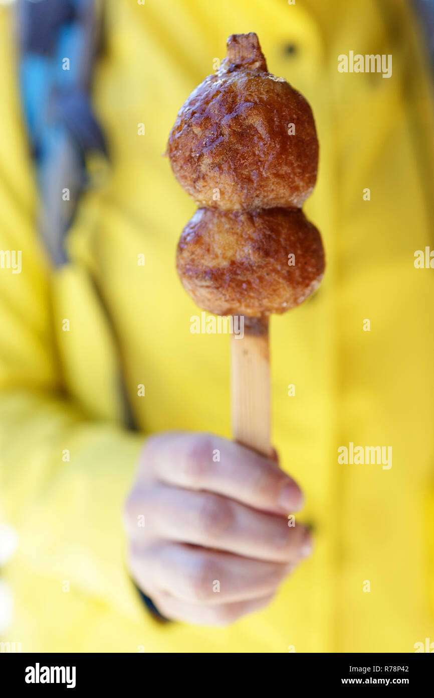 Woman in yellow jacket holding mochi balls on a stick with glazing ...