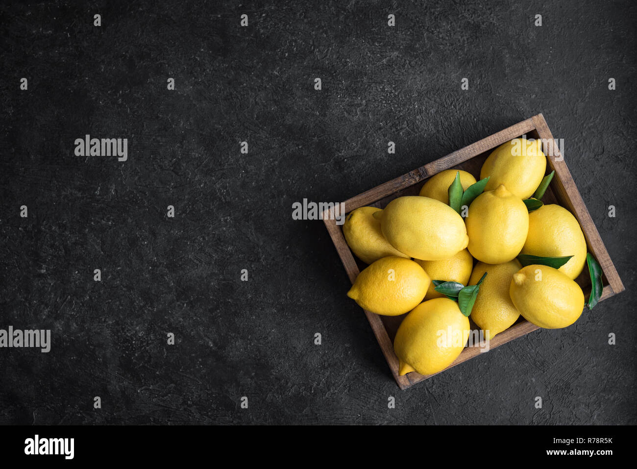 Lemons with green leaves in box on rustic black background, top view ...