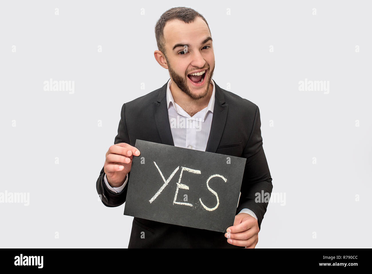 Happy young man in suit stands nd holds tablet with written word yes ...