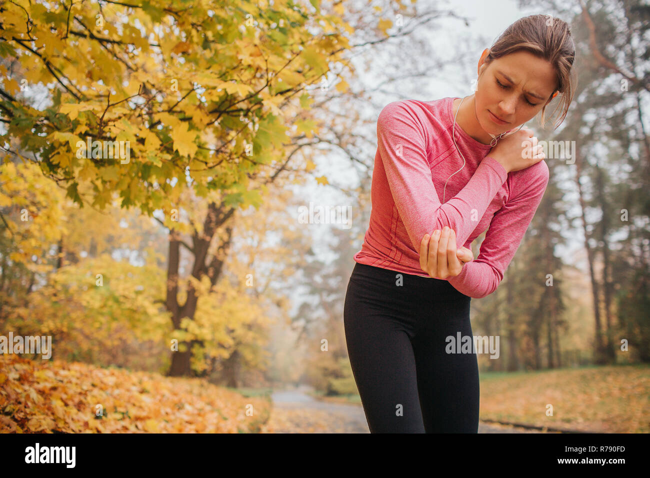 Sad and upset young female jogger stands in autumn park and hold hands ...
