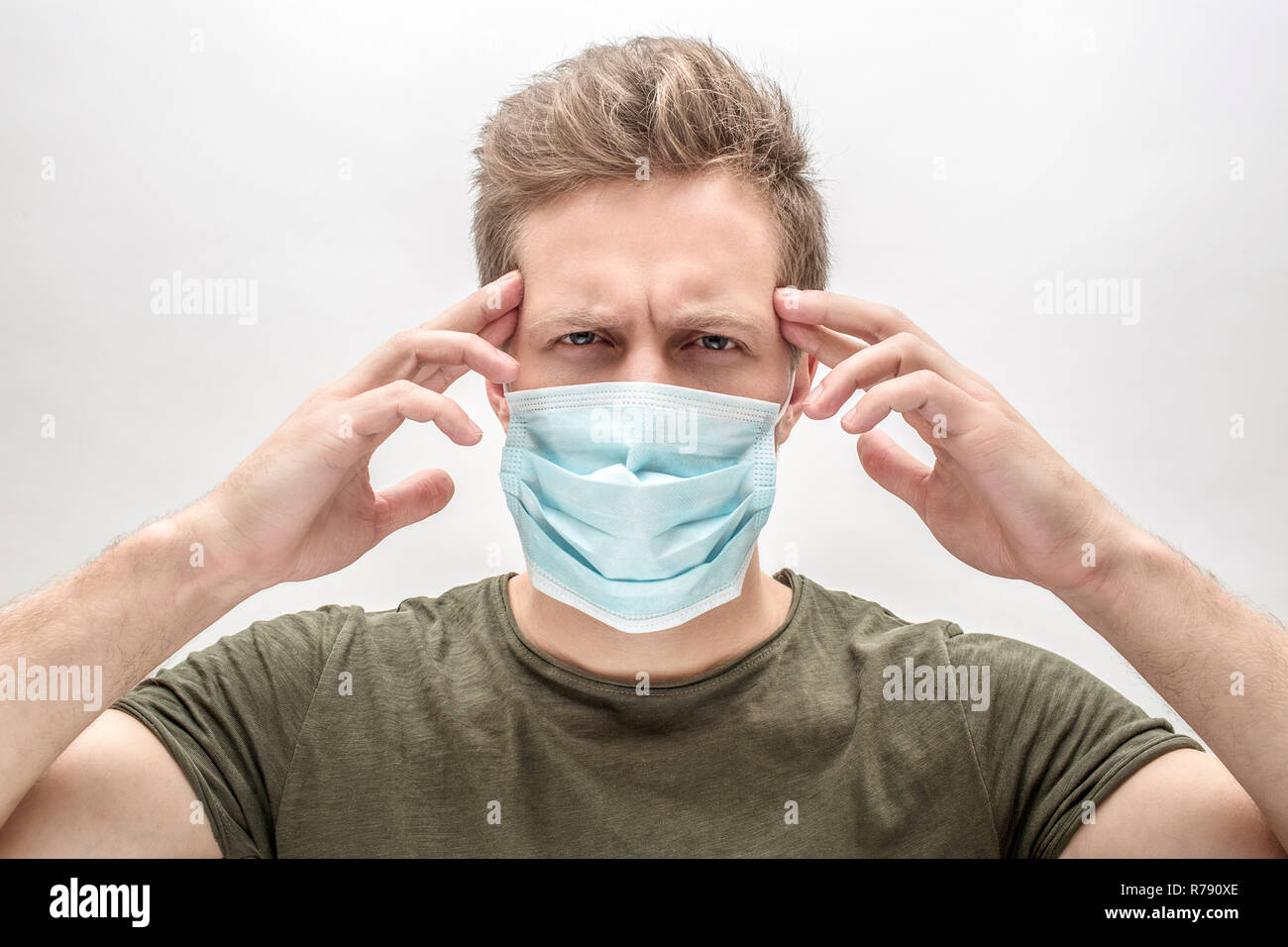 Young man in mask has headache. He hold hands on head. Guy feels pain ...