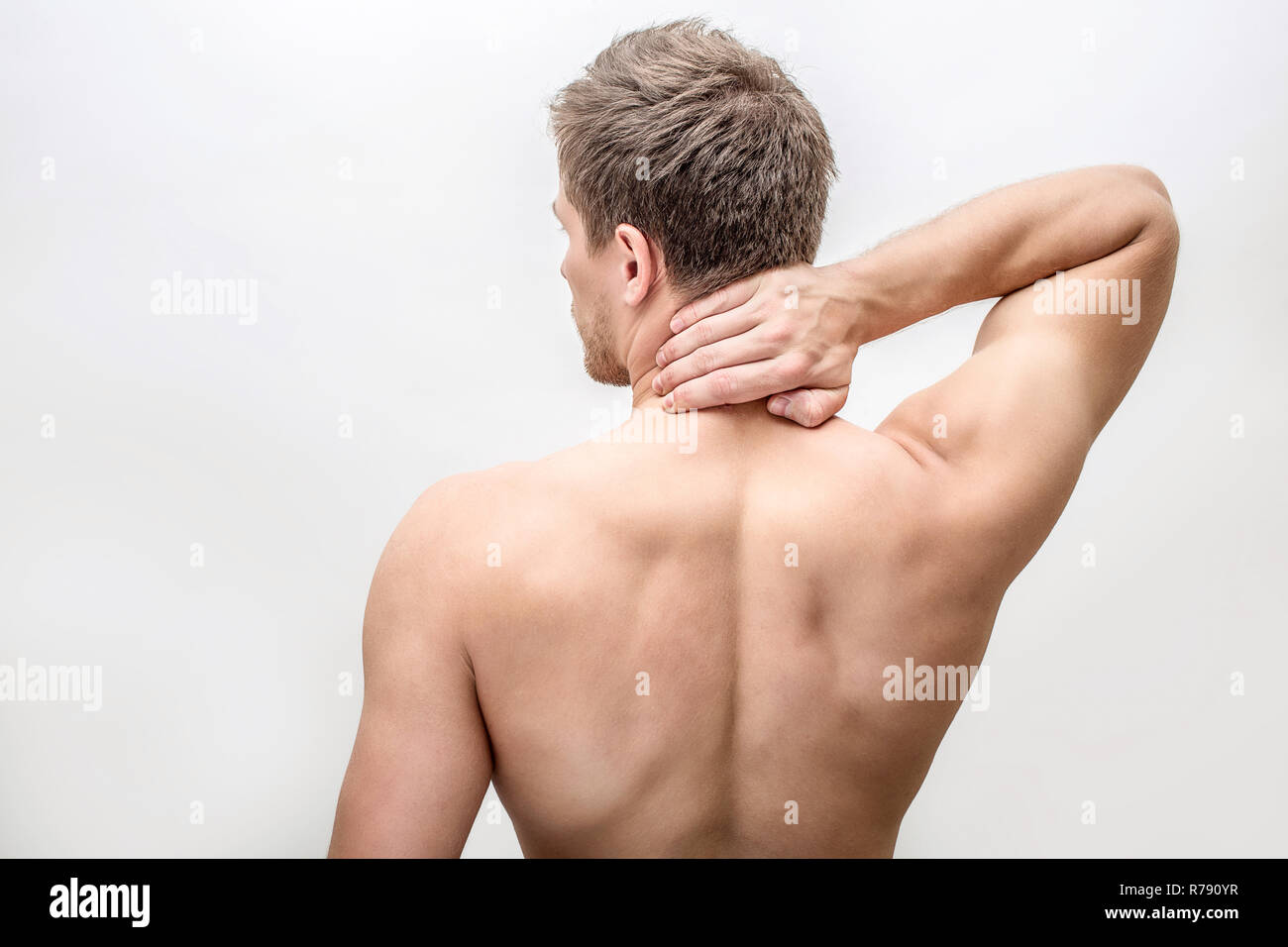 Shirtless young man stand and hold hand on neck. He feels pain there ...