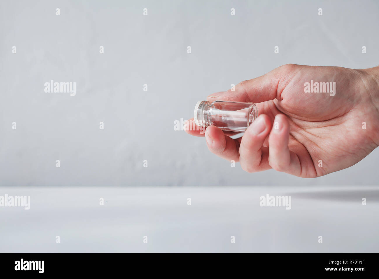Human hand holding an empty old glass vial on white blurred background ...