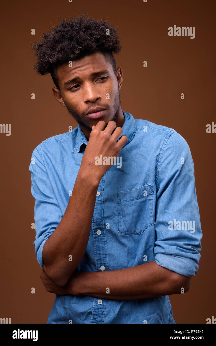 Young serious African man thinking against brown background Stock Photo ...
