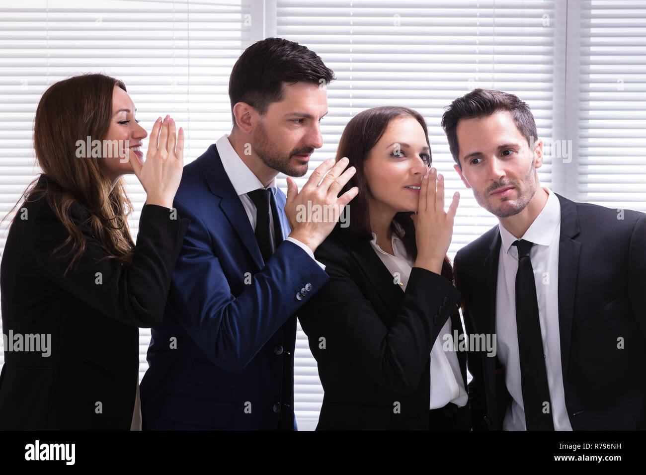 Businesspeople Gossiping Into Young Man's Ear Stock Photo - Alamy