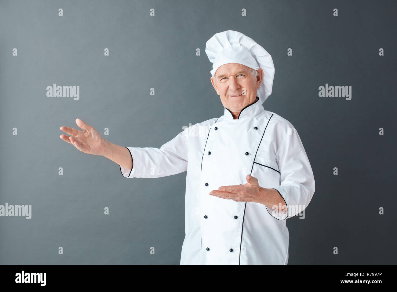 Senior chef studio standing isolated on gray looking camera showing ...
