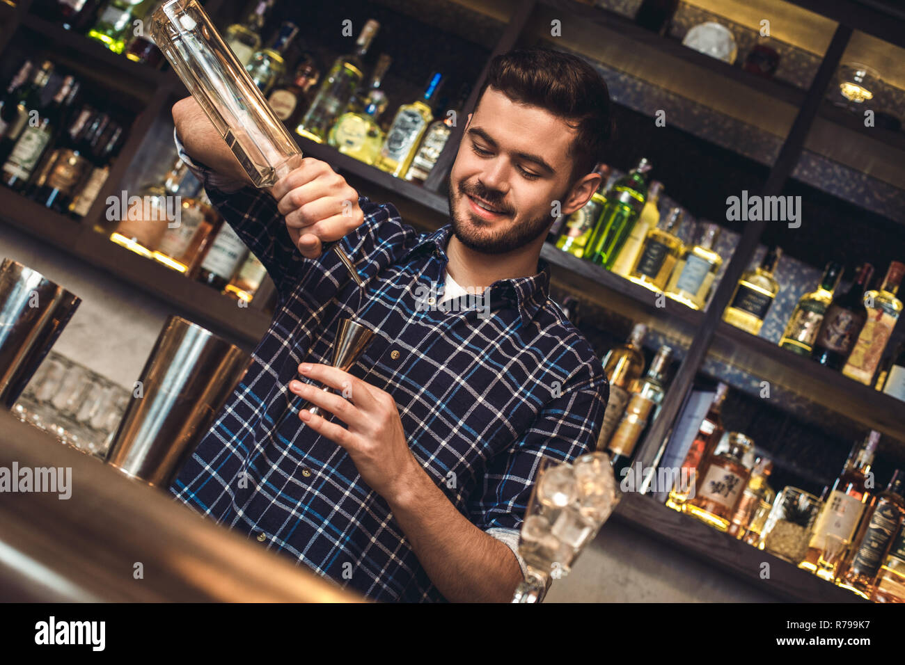 Young bartender standing at bar counter pouring alcohol into jigger happy Stock Photo - Alamy