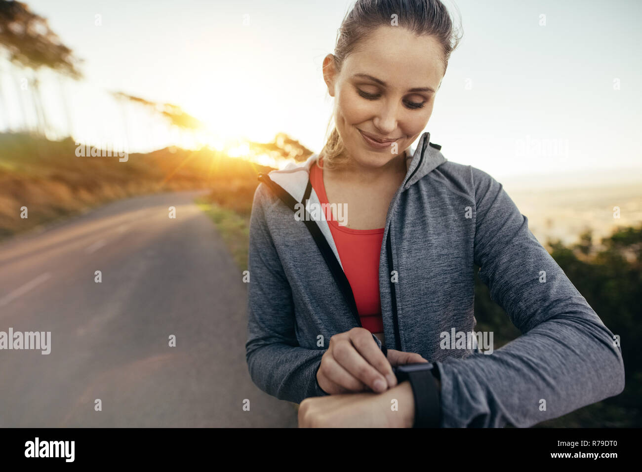 Smiling fitness woman checking time during her morning walk with sun in ...