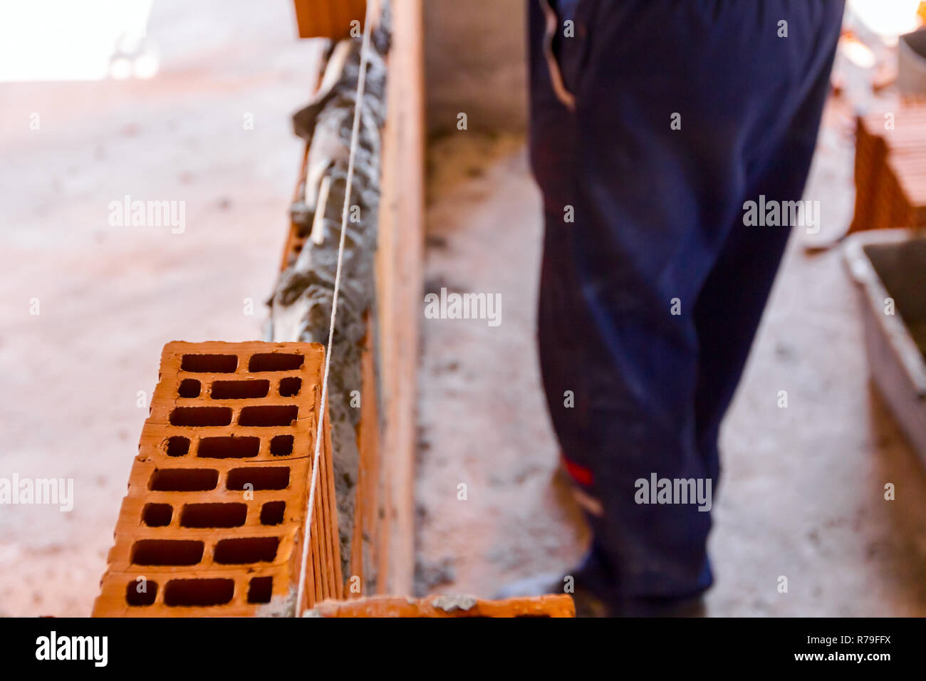 Mason, bricklayer worker is using red blocks to mount a wall next the ...