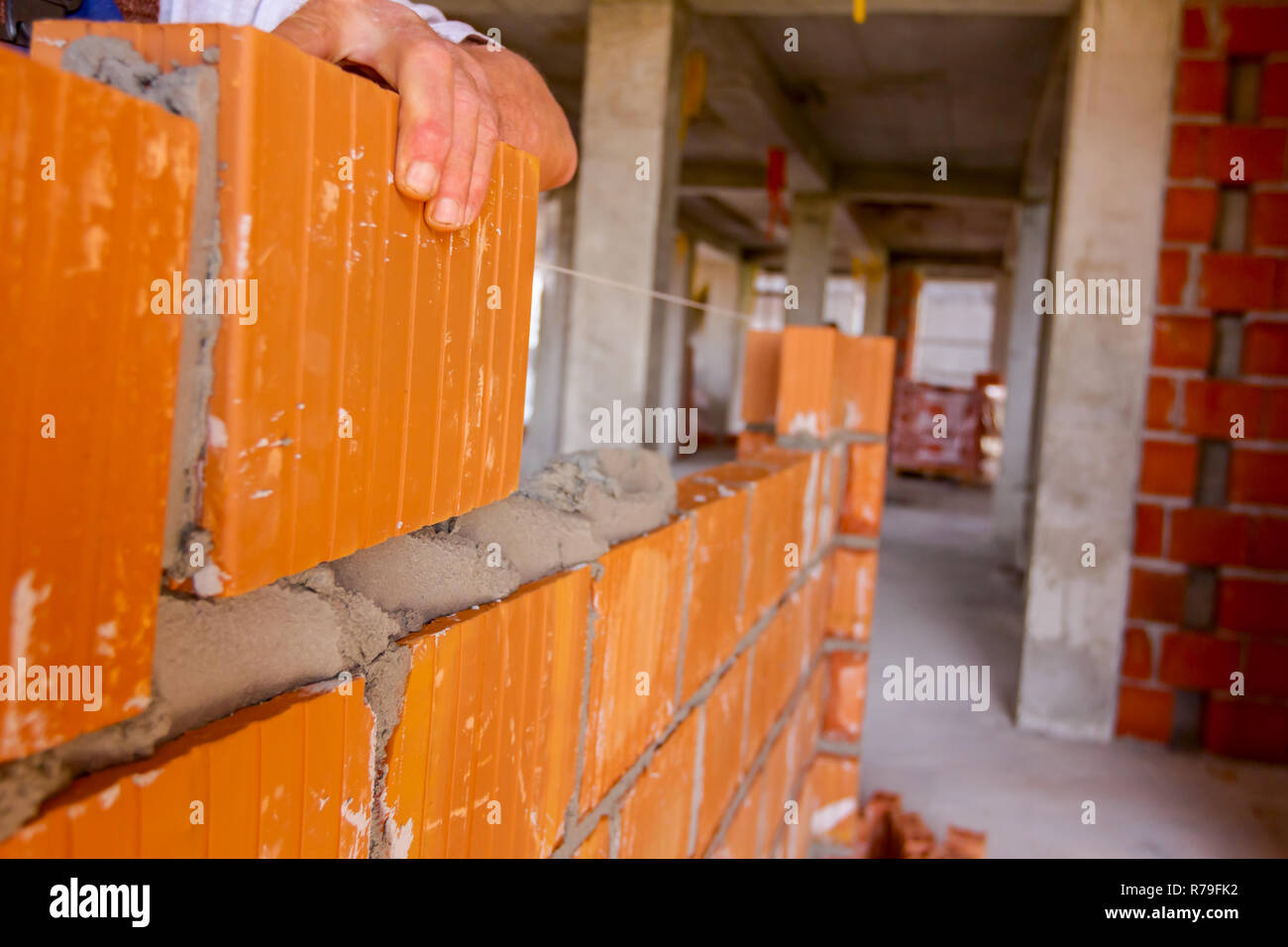 Mason, bricklayer worker is using red blocks to mount a wall next the ...